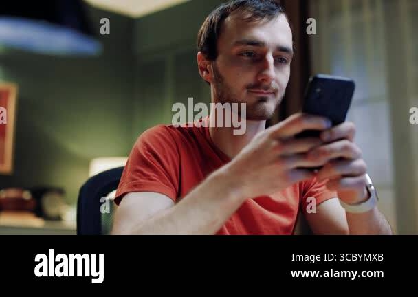 Zoom shot of young guy holding smartphone. Satisfied man looking at ...