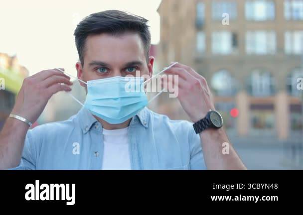 Close up of cheerful Caucasian man putting mask on his face to protect ...