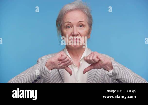 Older woman expressing disapproval with both thumbs down, frowning to ...