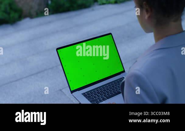 Rear view of a woman in a blazer using a laptop with a green screen ...