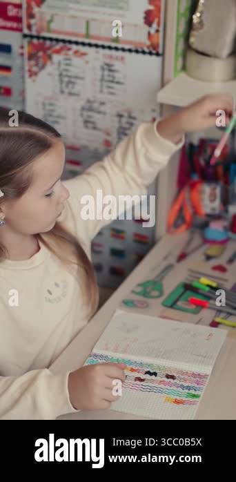 A young girl sits at her desk drawing in her notebook. She reaches for ...