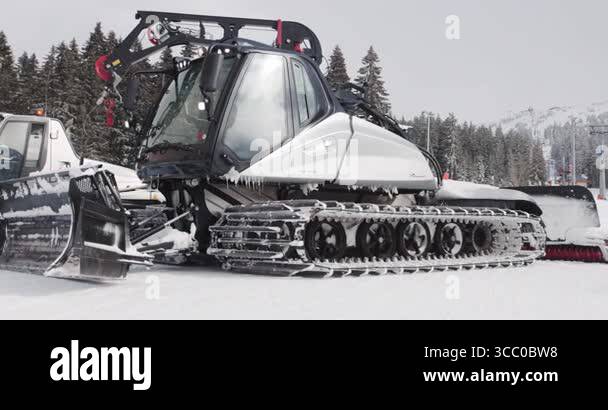 A snow groomer works across the wintery mountain terrain, smoothing ...