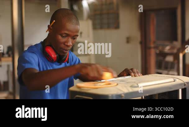 Guiding mid adult African American man feeding board through planer ...