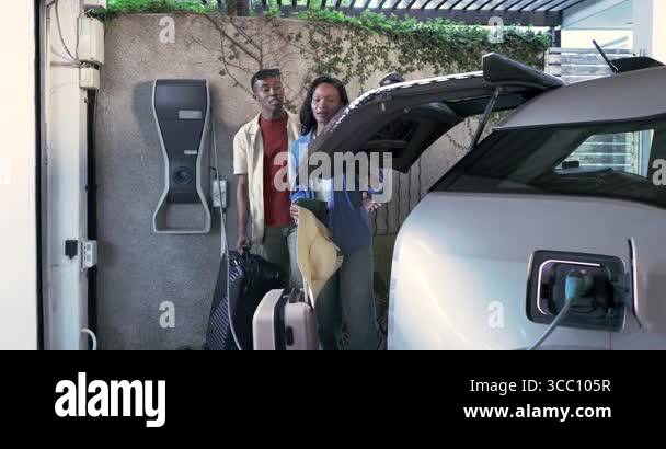 African American couple approaching carport stowing luggage in EV trunk ...