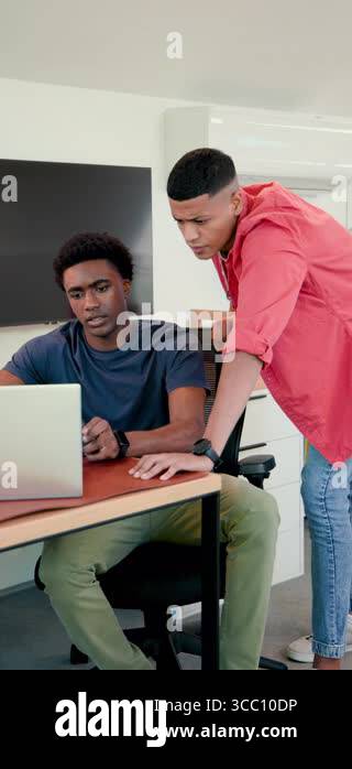 Diverse male coworkers leaning over laptop in office, typing then ...