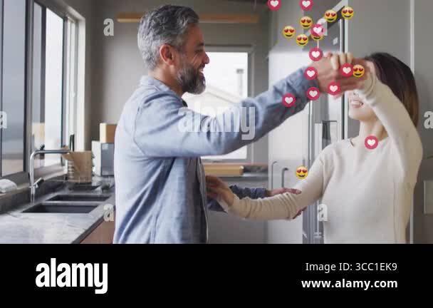 Lifestyle couple with man lifting partner hand causing twirl in kitchen with floating heart ...