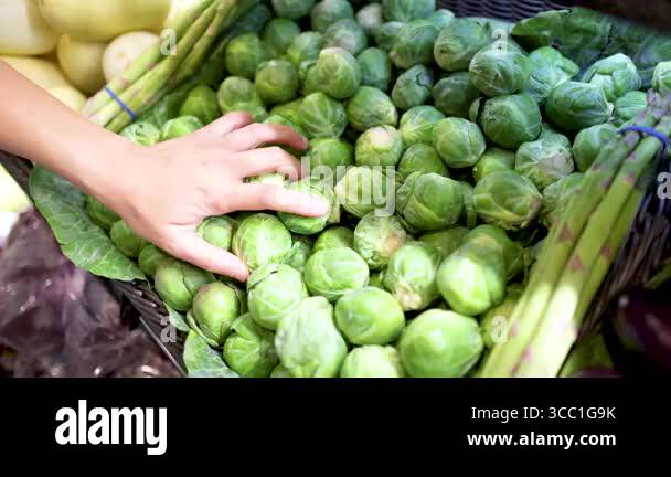 A hand picks fresh Brussels sprouts from a vibrant market display under ...