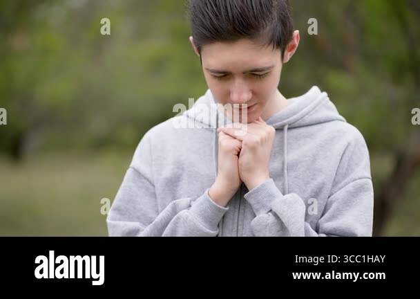 Portrait of teenage boy praying outdoors, worshiping God and embracing ...