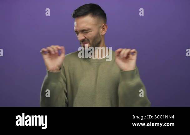 Young man in a sweater appears disgusted against a purple background ...