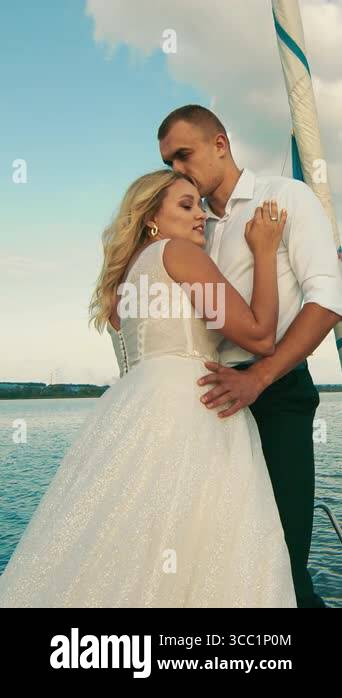 Bride rests her head on groom s chest aboard a sailing yacht. He gently ...