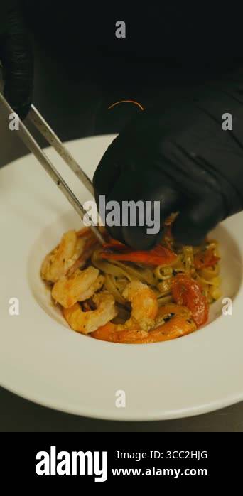 A skilled chef is plating an exquisite shrimp pasta dish with tongs for ...