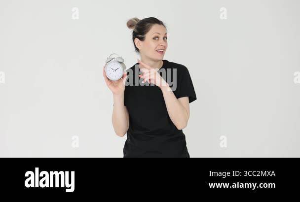 Smiling woman in black shirt holds classic alarm clock while looking ...