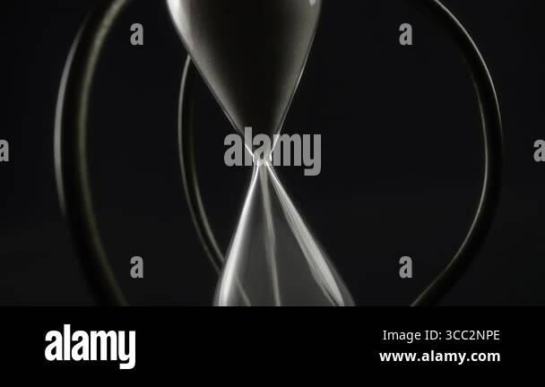 Rotating hourglass with pouring sand on black background. Abstract ...