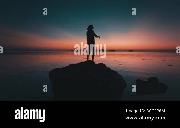 Watching sunset from rocky shoreline. Silhouette of tourist standing on ...