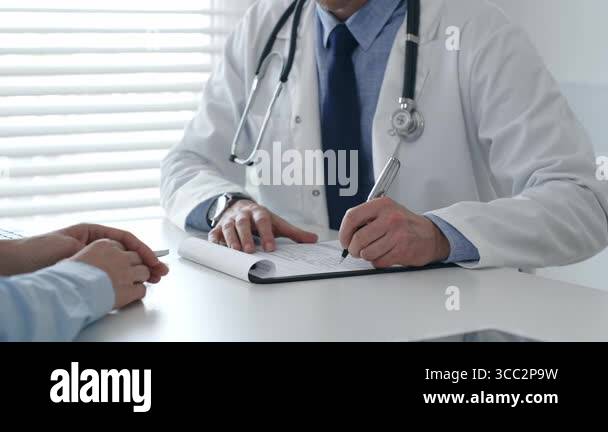 Doctor writing notes on a clipboard while talking with patient in ...