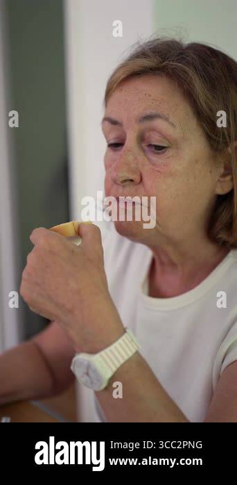 Older woman chewing bread while seated at table, eyes looking down in ...