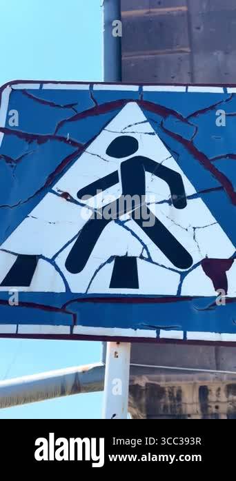 Old crosswalk with cracked paint. A sign with a person walking on it is ...