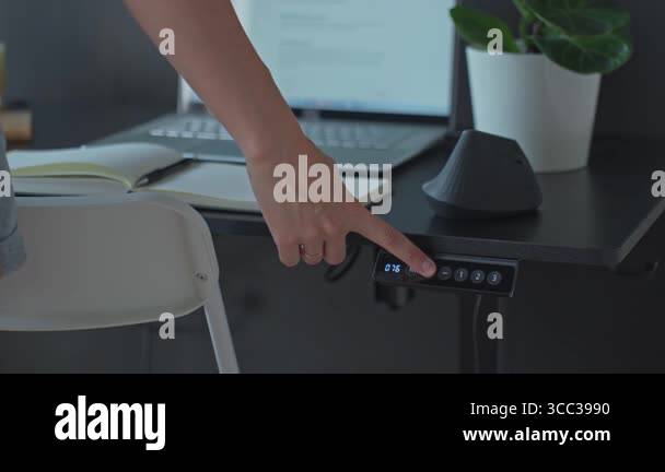 Woman raising height of electric standing desk by pressing control ...