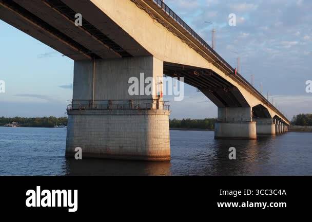 Concrete bridge structure over wide river under cloudy sky at sunset ...