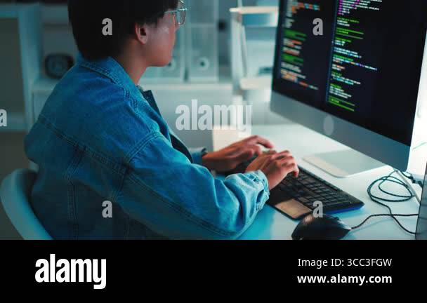 Software developer using keyboard focused on debugging programming code on dual monitor setup in ...