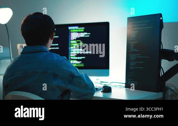 Programmer working late in a cybersecurity or software development environment using multiple ...