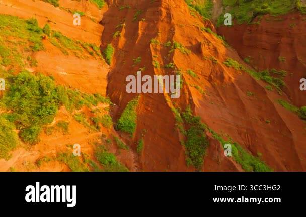 Drone view of vibrant greenery contrasting sharply with eroded red clay ...