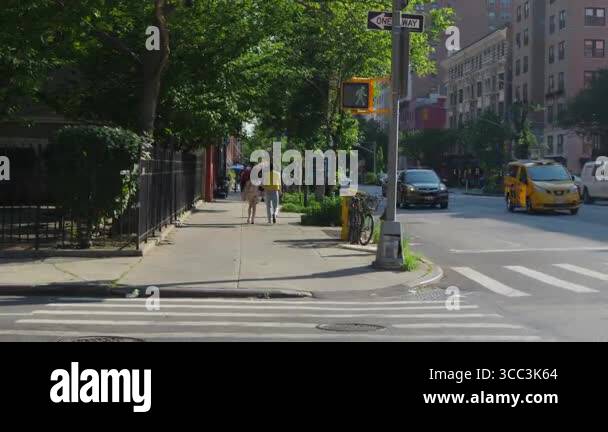 A typical New York City street scene, featuring pedestrians and yellow taxis under a clear blue ...