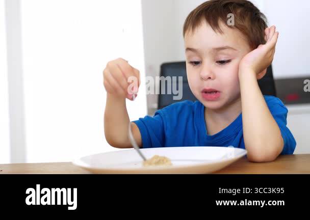 Child is eating a meal at home table. A young boy is sitting at a table ...