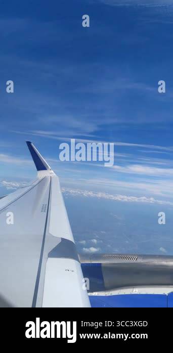 Airplane wing and engine visible flying above dark Blue sky and cities ...