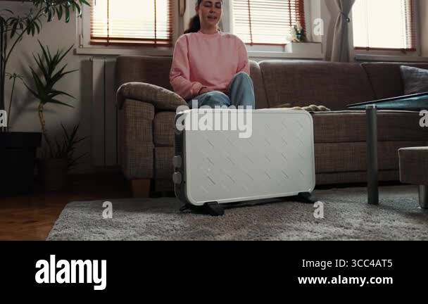 Winter heating season. Young smiling caucasian woman sits on sofa, put ...