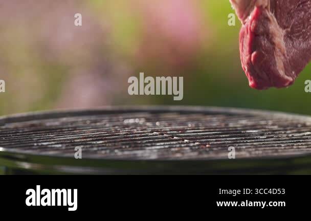 A cook put fresh raw beef steak on charcoal grill in backyard garden ...