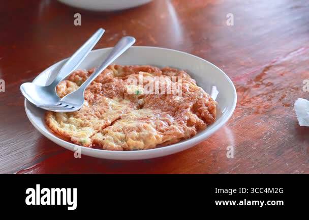 A Thai-style omelette served on a rustic wooden table, captured in ...