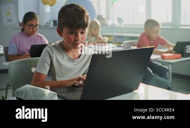 Elementary School Boy Sitting at Desk, Using Laptop in Classroom. Team ...