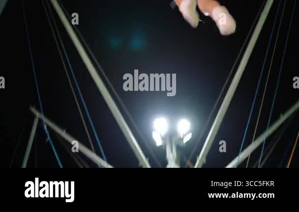 Young girl flipping upside down in air on nighttime bungee trampoline ...