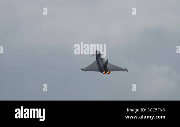 Military fighter jet flying upward with visible afterburners and cloudy ...