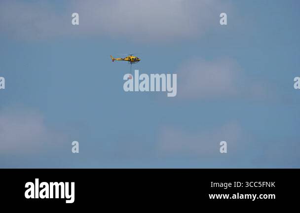 Yellow helicopter flying in clear blue sky carrying red bambi bucket ...