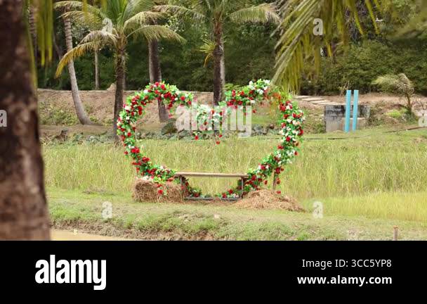 A heart-shaped floral frame stands in a lush, tropical setting with ...