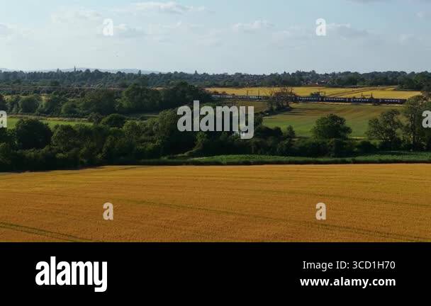 Passenger train traveling through hilly farmland under soft daylight ...