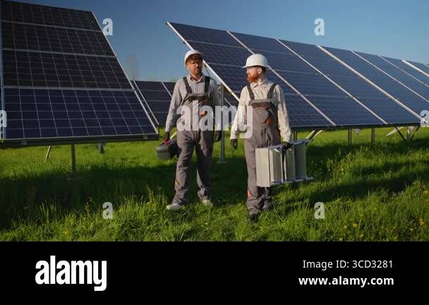 Professional engineers walking between rows of solar panels, carrying ...
