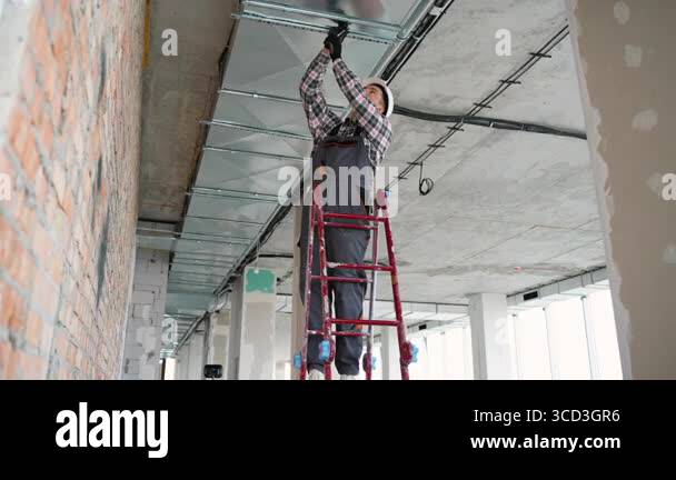 Skilled technician in work uniform installs ventilation ducts in a ...