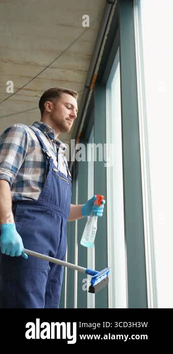 Professional window cleaner wearing blue protective workwear cleaning ...