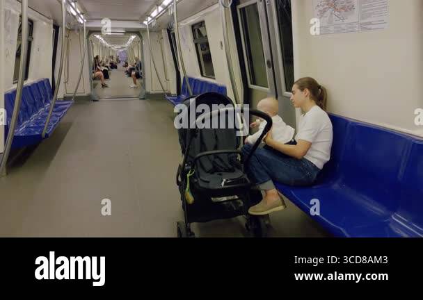 A mother is seated on a blue bench in a subway train, holding her baby ...