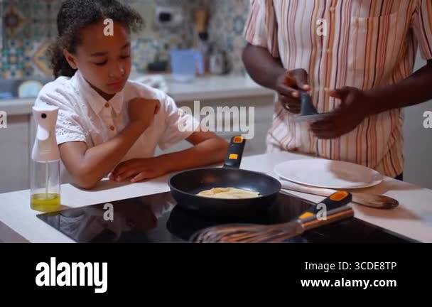 African American father man hand frying pancakes together with daughter ...