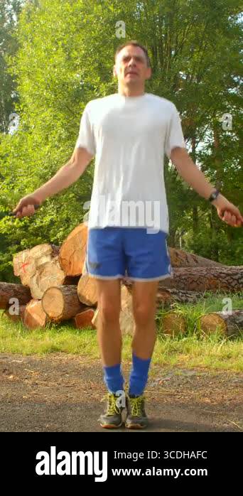 A man in a white shirt and blue shorts jumps rope outdoors, showing ...