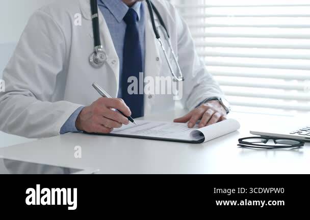 Male physician wearing a lab coat and stethoscope, sitting at a desk in ...