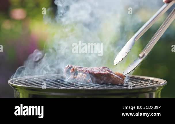 A cook turn around and put freshly grilled beef steak on charcoal grill ...