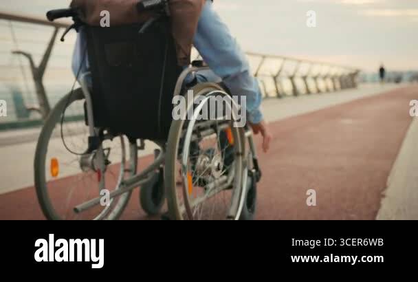 Man propels wheelchair forward turning wheels on bridge walkway with ...
