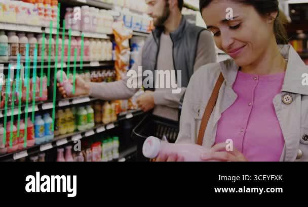 Woman reaching pink drink in store aisle reading nutrition label while ...