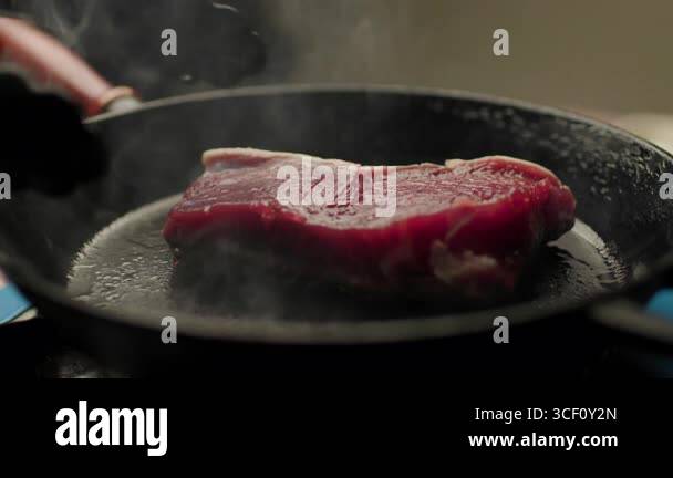 Close-up shot of a beef steak sizzling on a hot frying pan, roasting to ...
