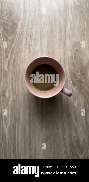 A cup of coffee sits on a wooden table. The coffee is hot and has a ...